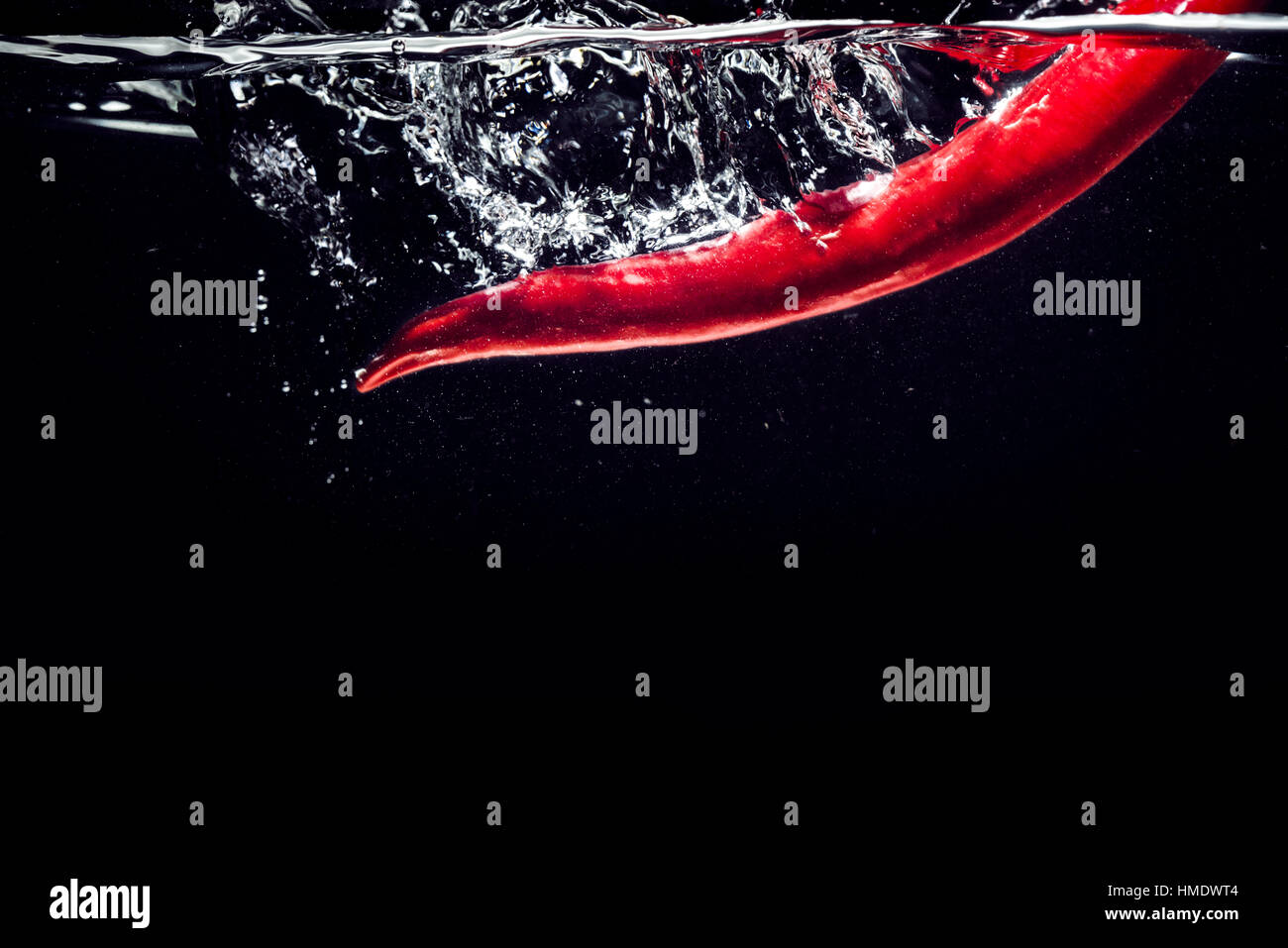 Red hot chili pepper splashing into water isolated on the black ...