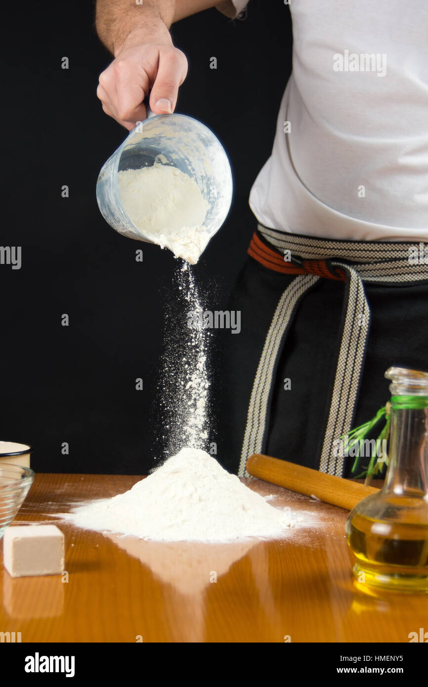Man pouring flour from the measure bowl on the table Stock Photo - Alamy