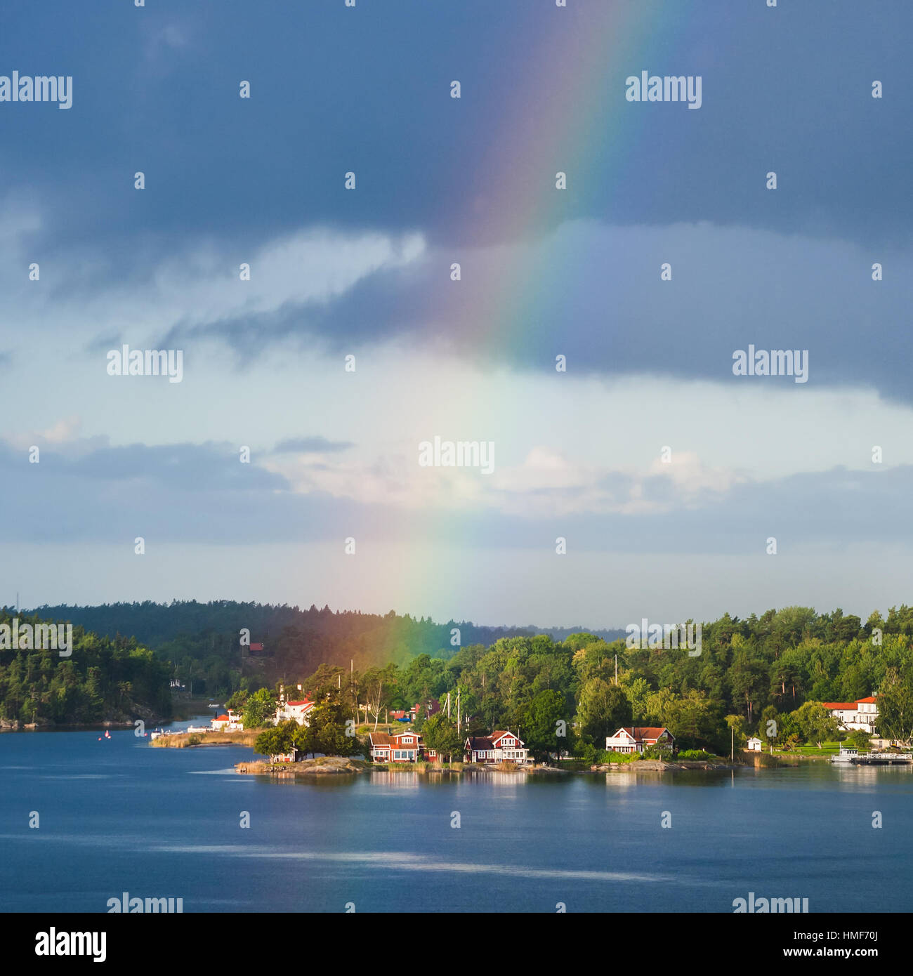 green coast of Baltic Sea with village and rainbow in blue sky in sunny ...