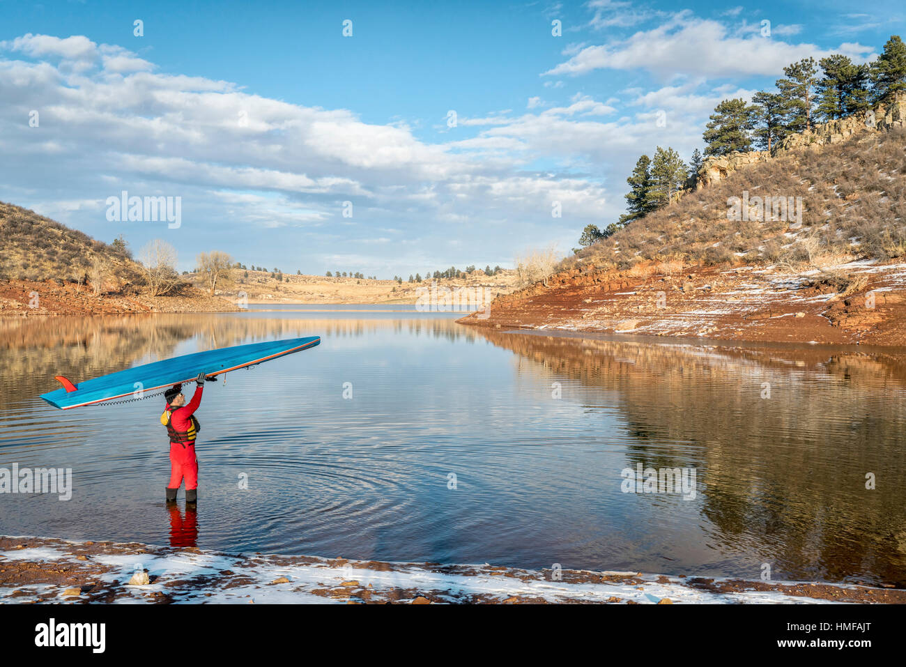 male paddler in drysuit is launching stand up paddleboard on a lake in ...