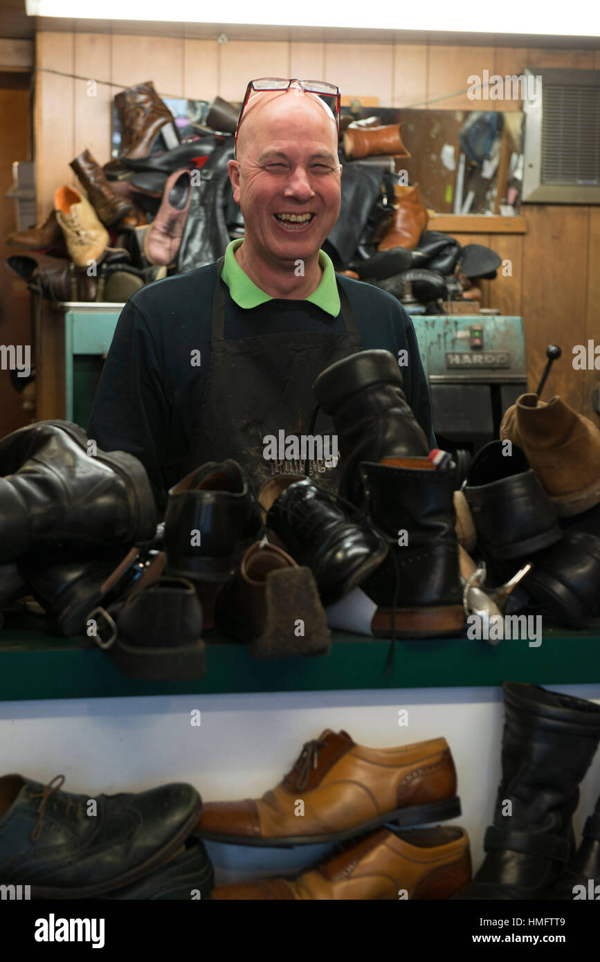 an old fashioned shoe repair / cobbler fixes shoes in his busy shop ...
