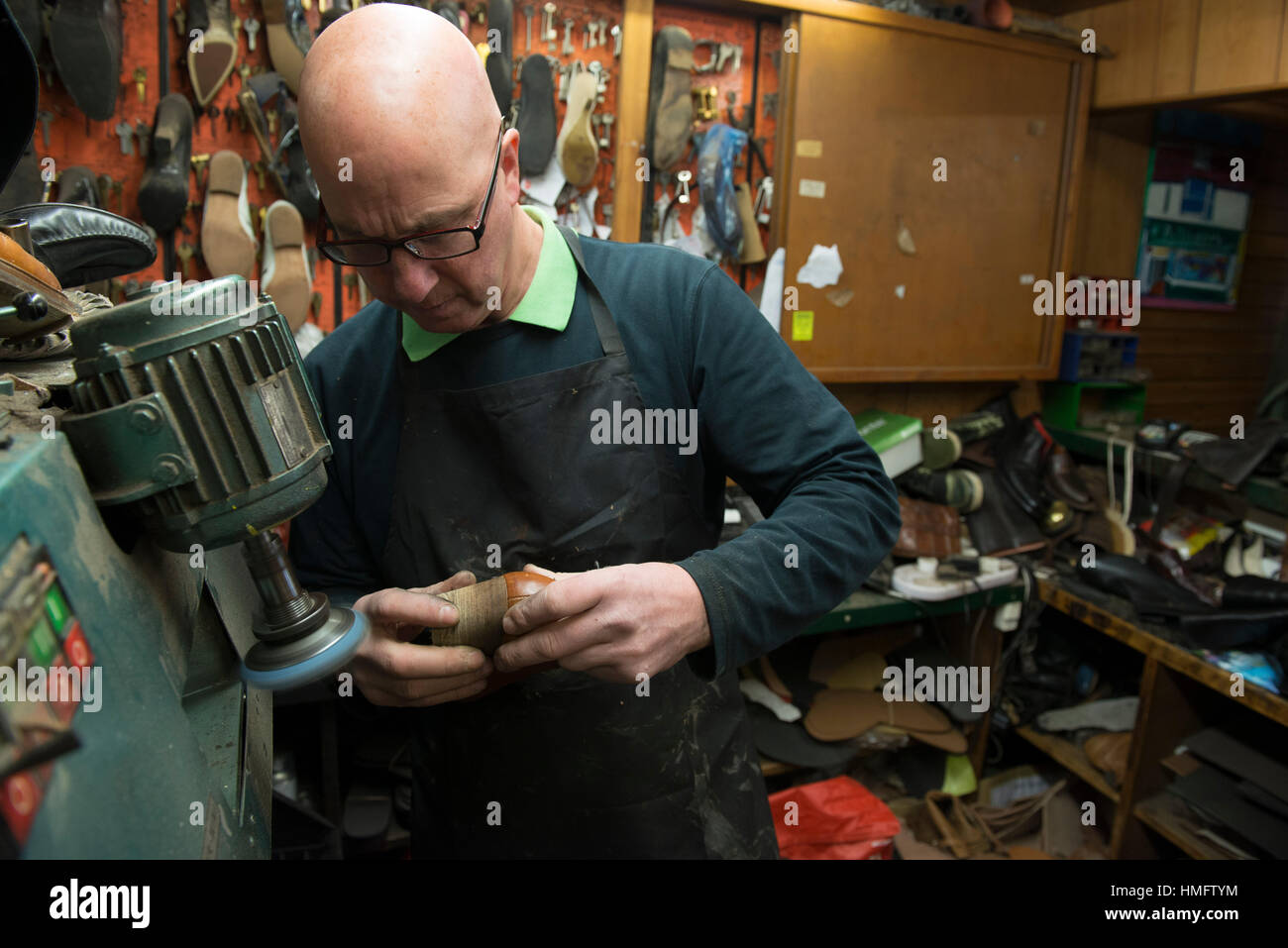 an old fashioned shoe repair / cobbler fixes shoes in his busy shop ...