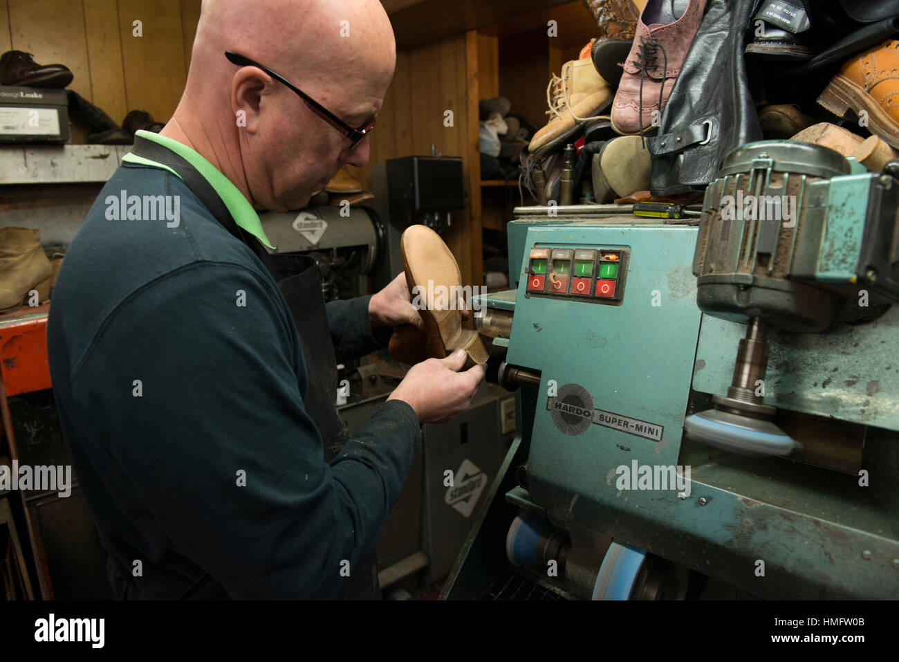 an old fashioned shoe repair / cobbler fixes shoes in his busy shop ...
