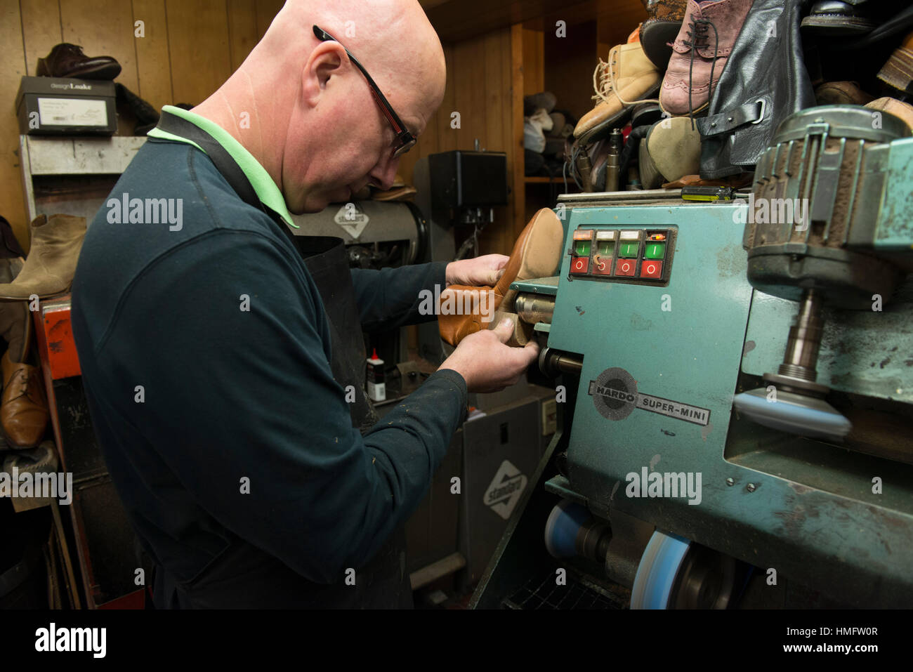 an old fashioned shoe repair / cobbler fixes shoes in his busy shop ...