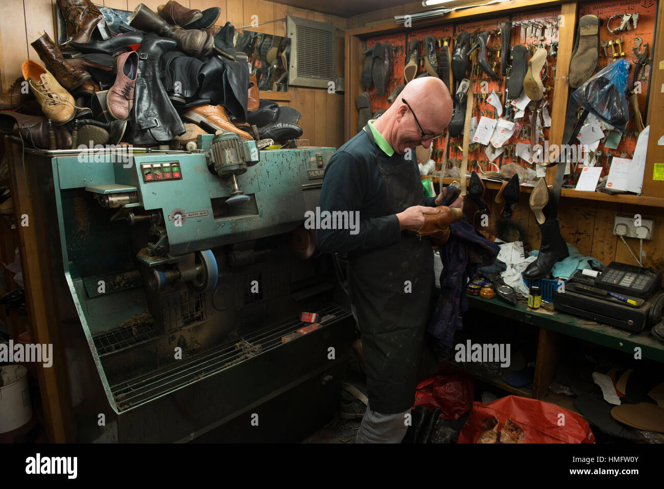 an old fashioned shoe repair / cobbler fixes shoes in his busy shop ...