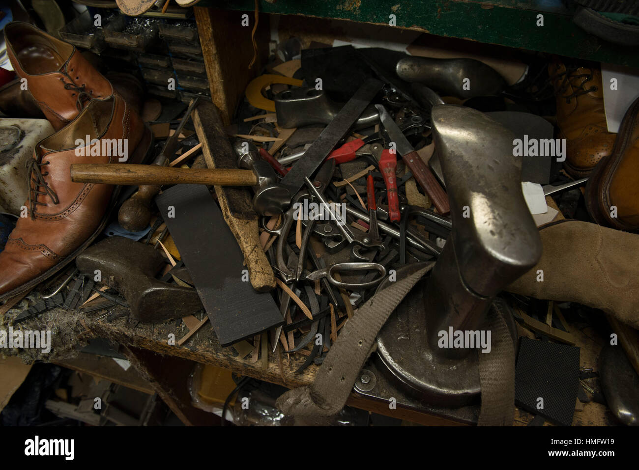 an old fashioned shoe repair / cobbler fixes shoes in his busy shop ...