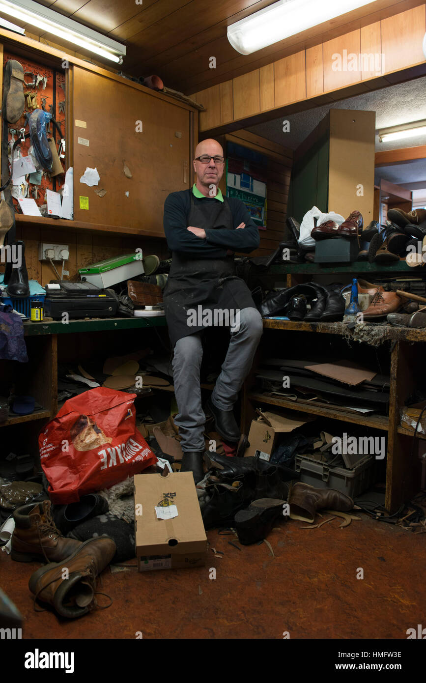an old fashioned shoe repair / cobbler fixes shoes in his busy shop ...