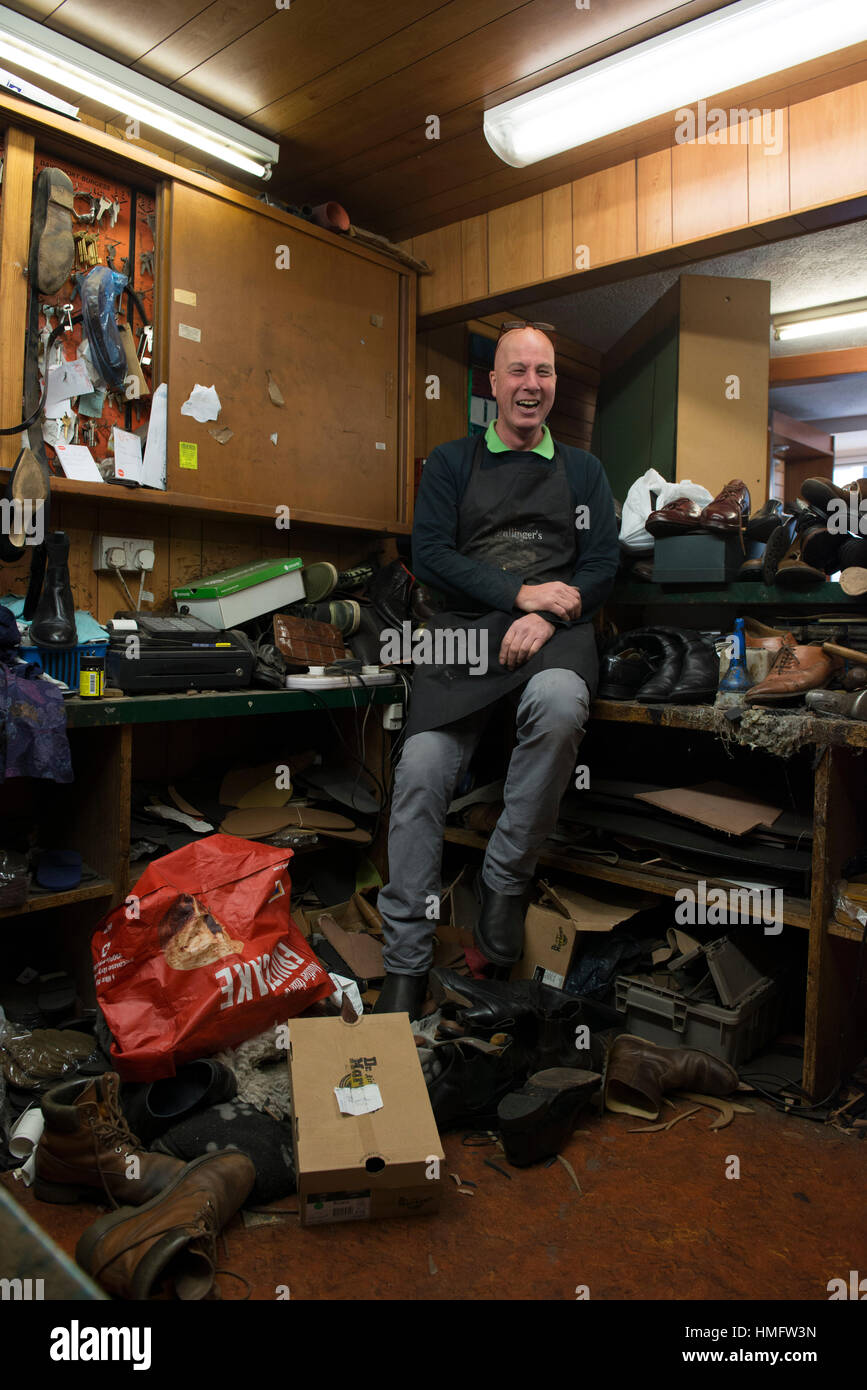 an old fashioned shoe repair / cobbler fixes shoes in his busy shop ...
