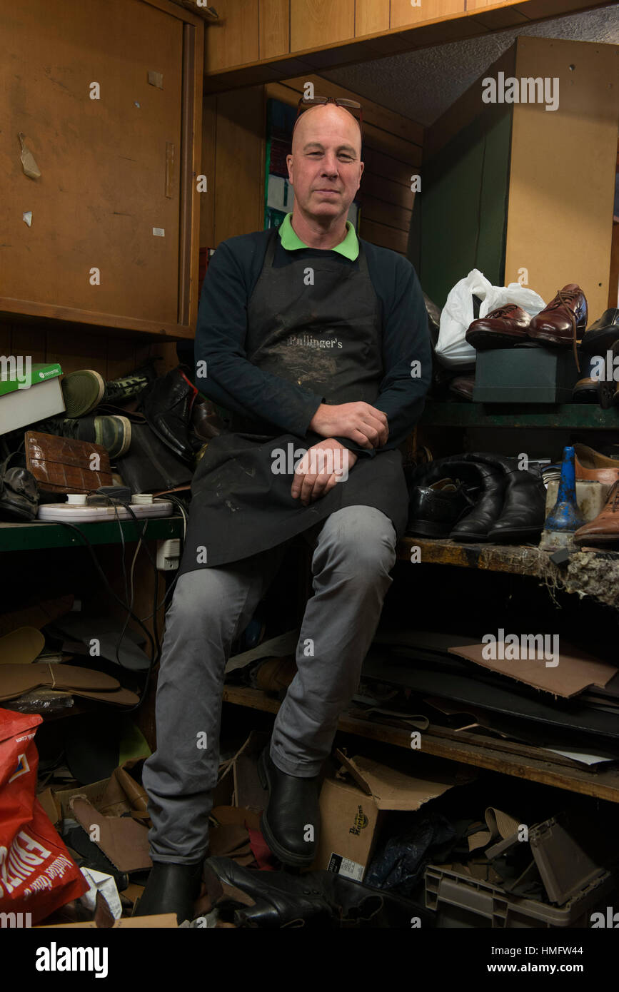 an old fashioned shoe repair / cobbler fixes shoes in his busy shop ...