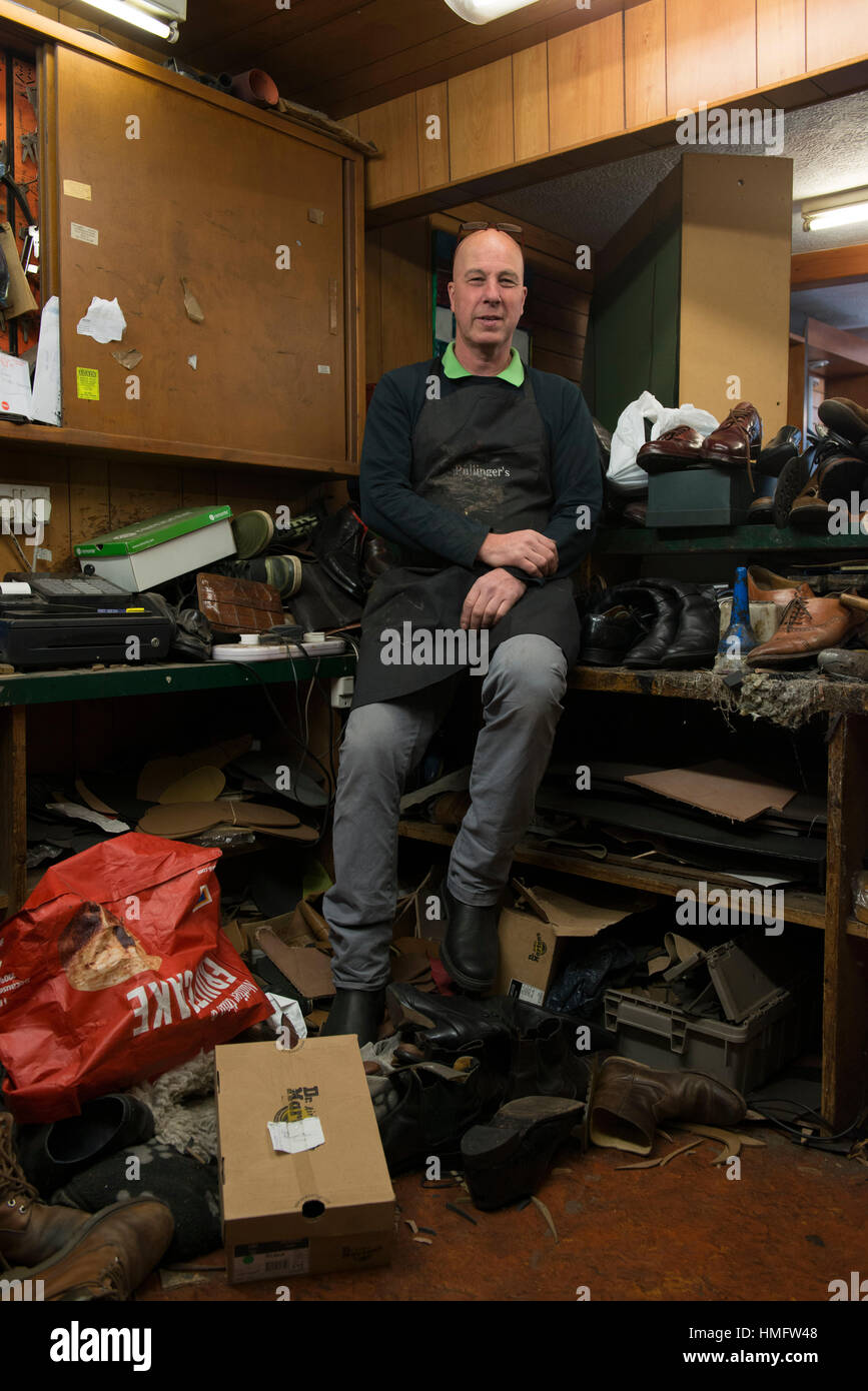 an old fashioned shoe repair / cobbler fixes shoes in his busy shop ...