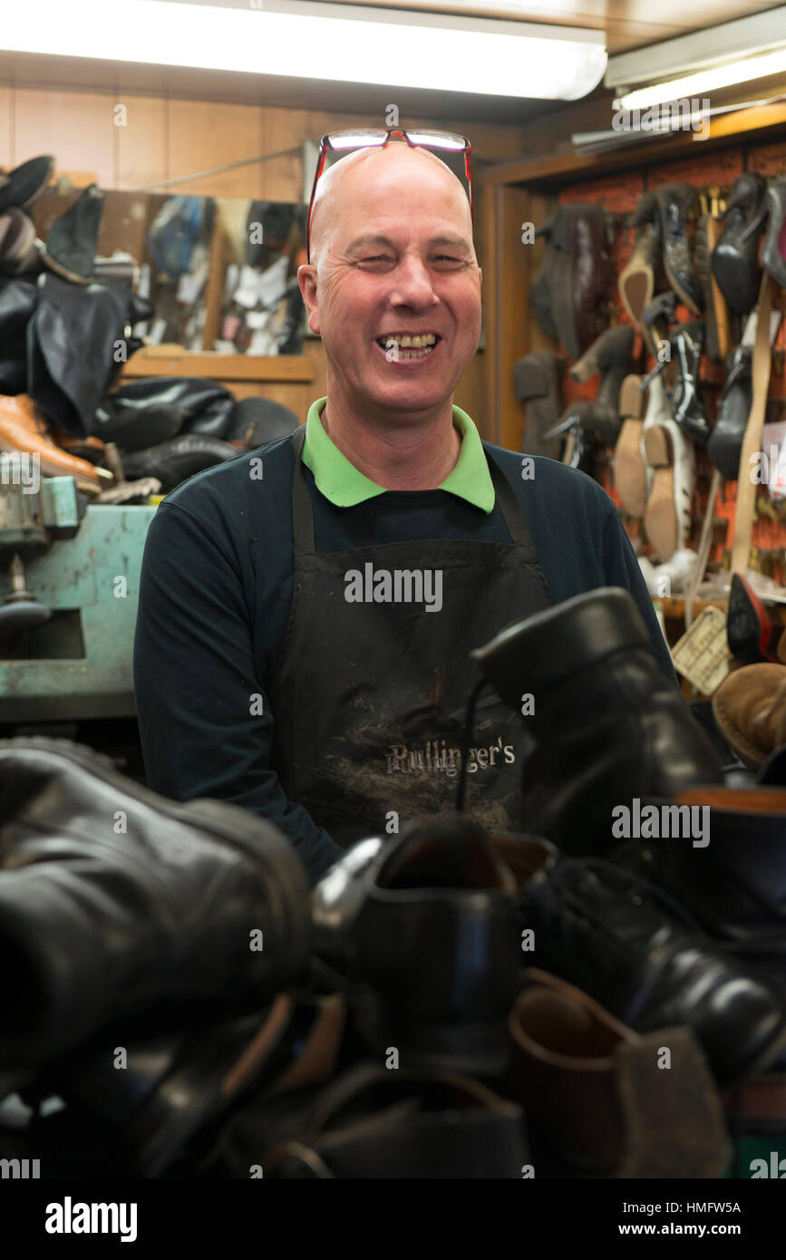 an old fashioned shoe repair / cobbler fixes shoes in his busy shop ...