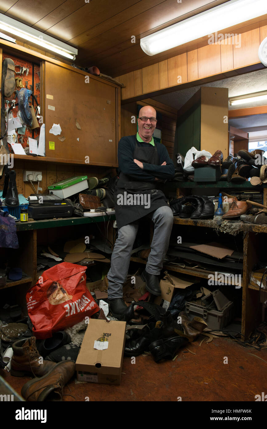 an old fashioned shoe repair / cobbler fixes shoes in his busy shop ...