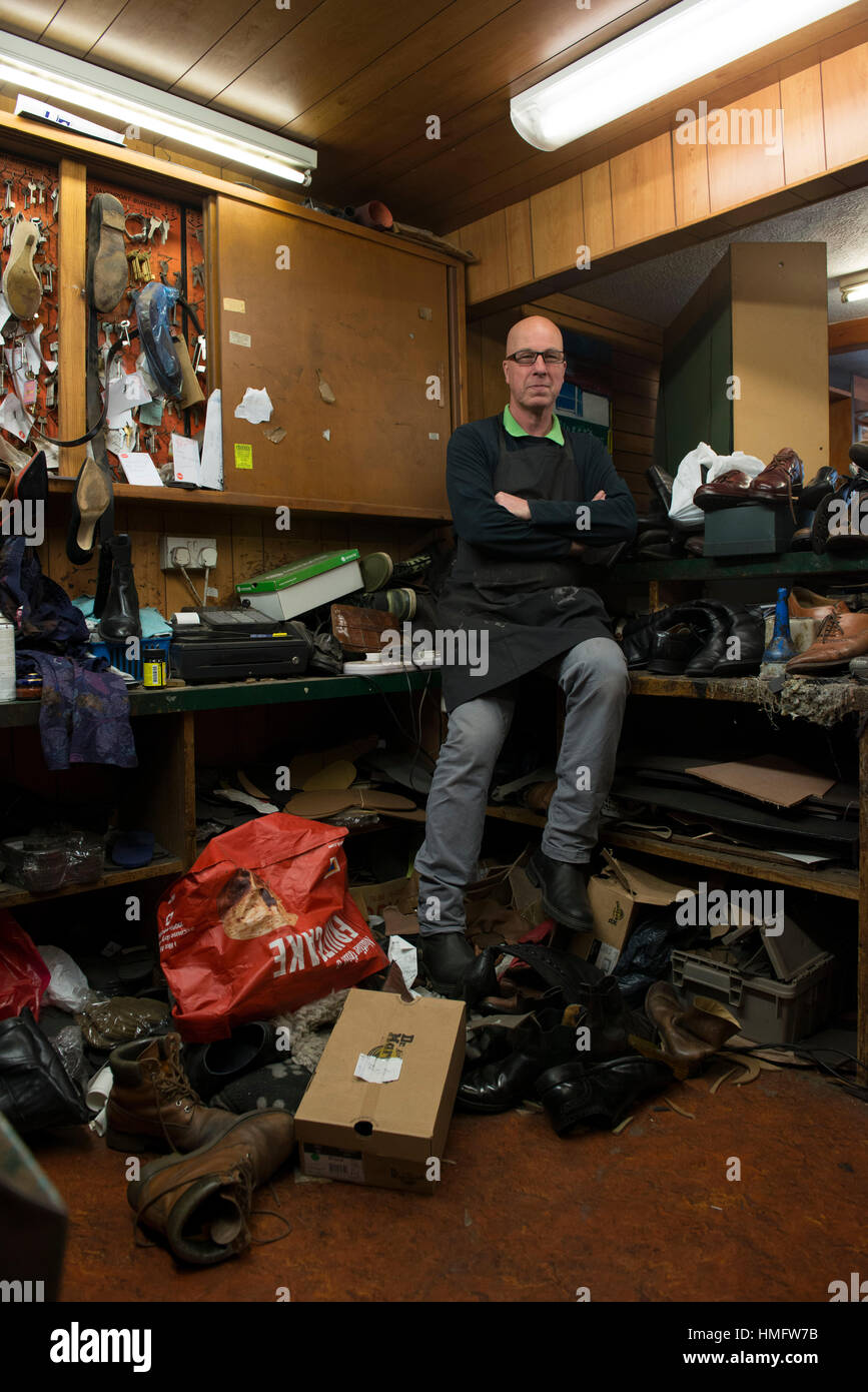 an old fashioned shoe repair / cobbler fixes shoes in his busy shop ...