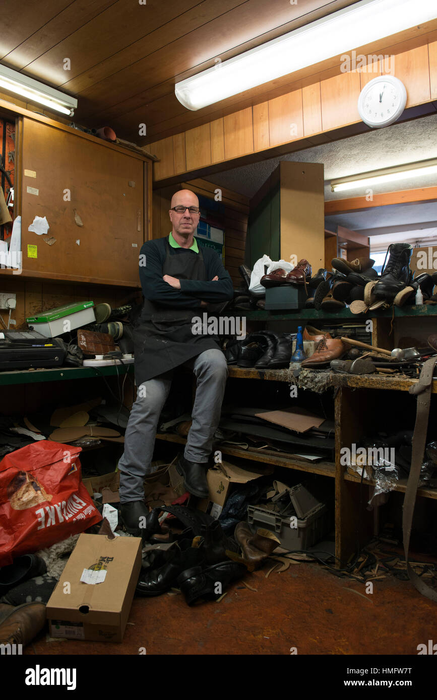 an old fashioned shoe repair / cobbler fixes shoes in his busy shop ...