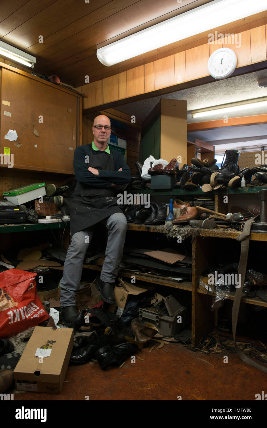 an old fashioned shoe repair / cobbler fixes shoes in his busy shop ...