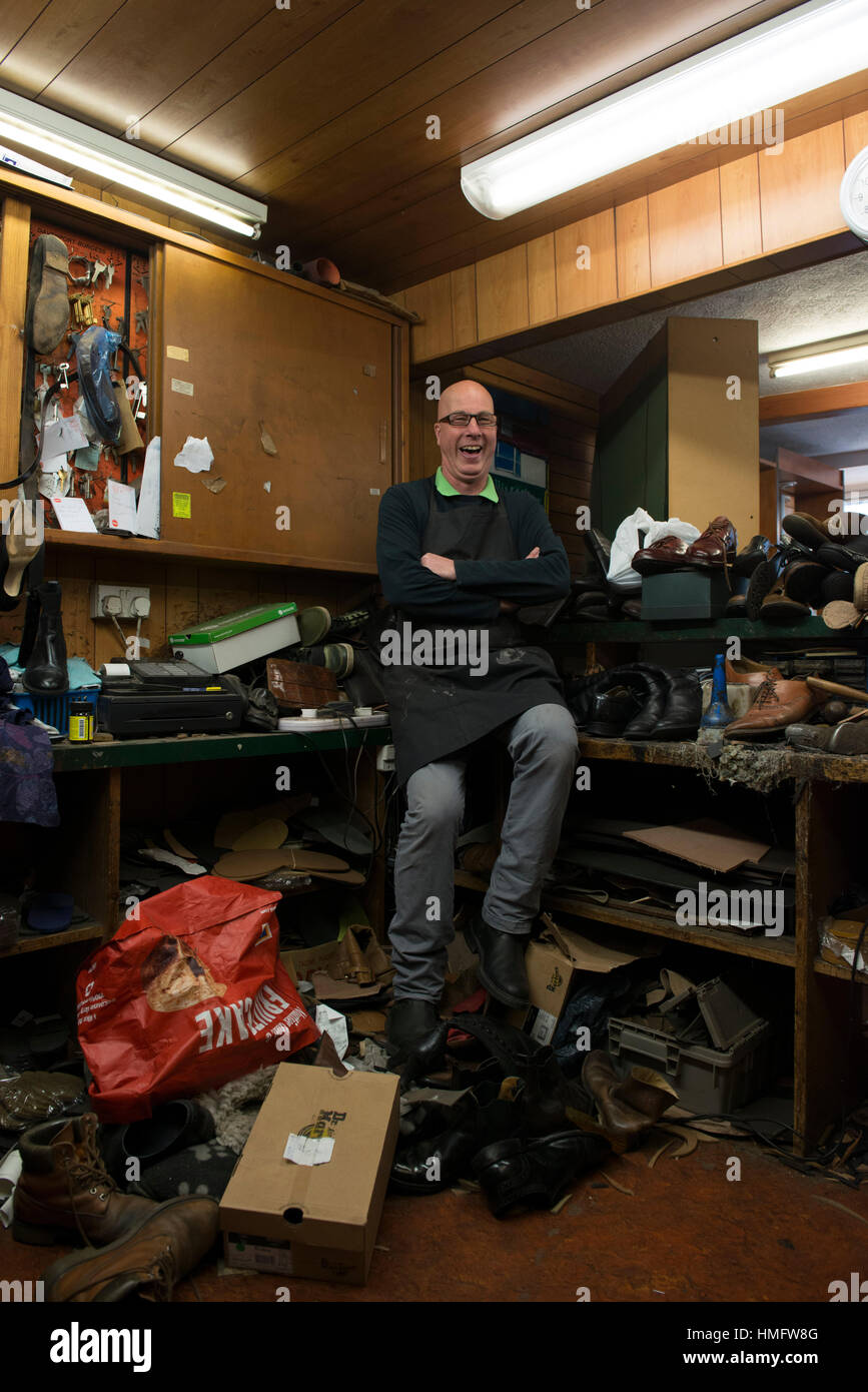 an old fashioned shoe repair / cobbler fixes shoes in his busy shop ...