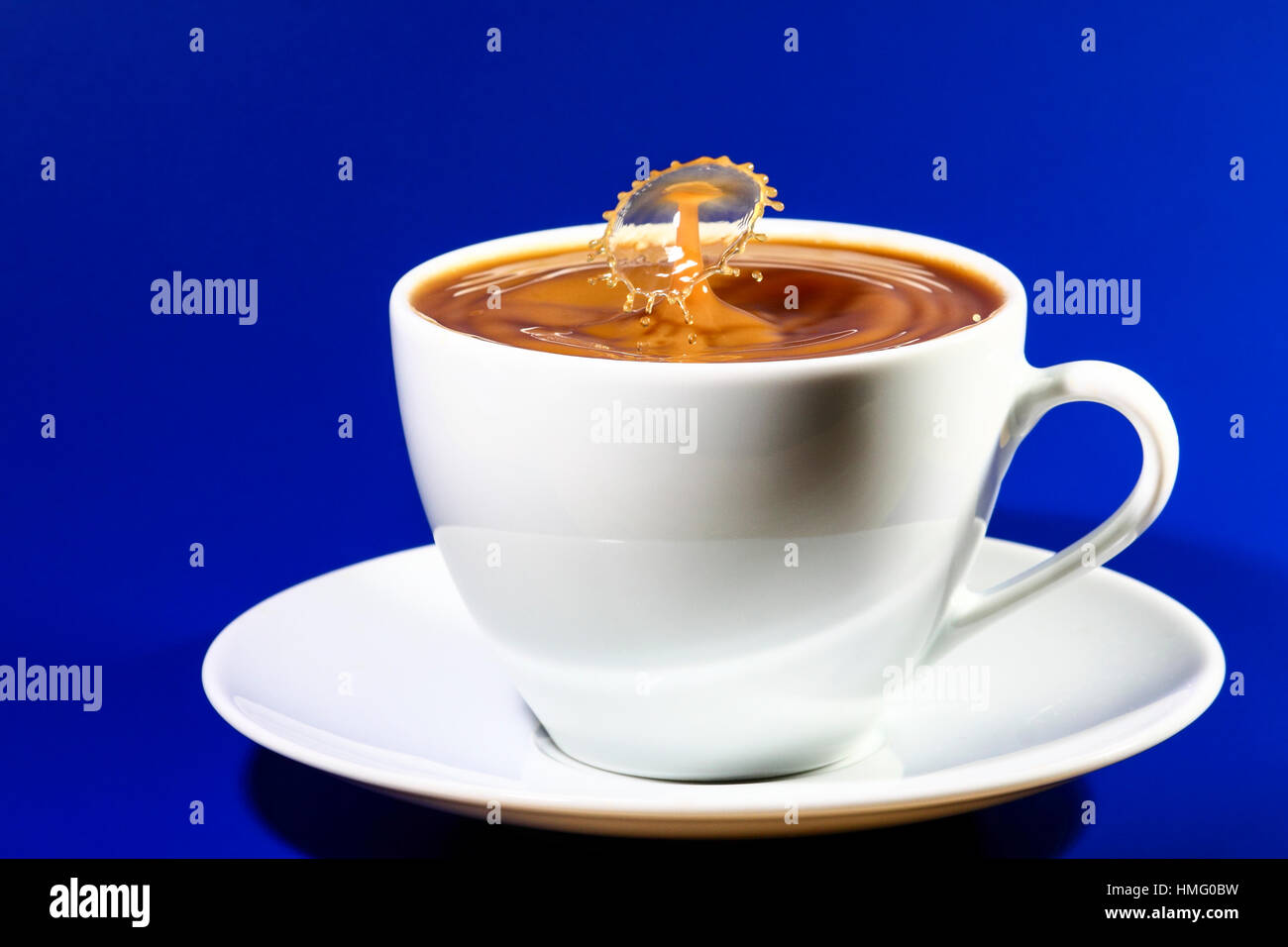 Tea splashing in to a white teacup and saucer isolated on a blue ...