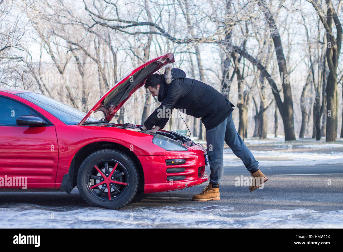 Man in trouble with his broken car .He is looking at engine under hood ...