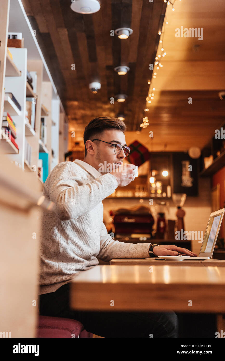 Photo of young concentrated man sitting in cafe while drinking coffee ...