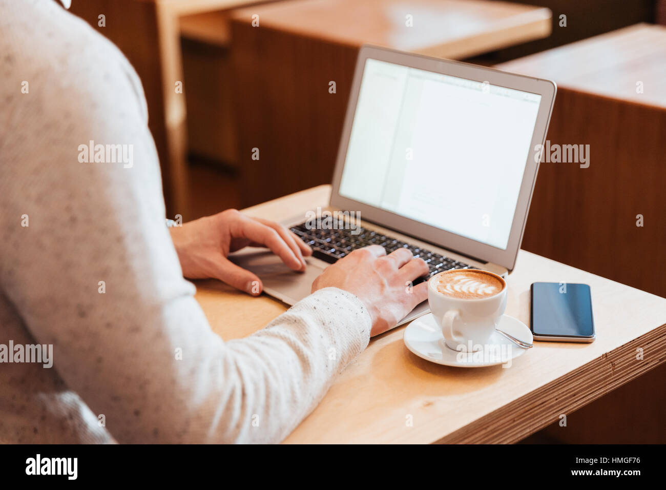 Back view cropped image of young man sitting in cafe near coffee while ...