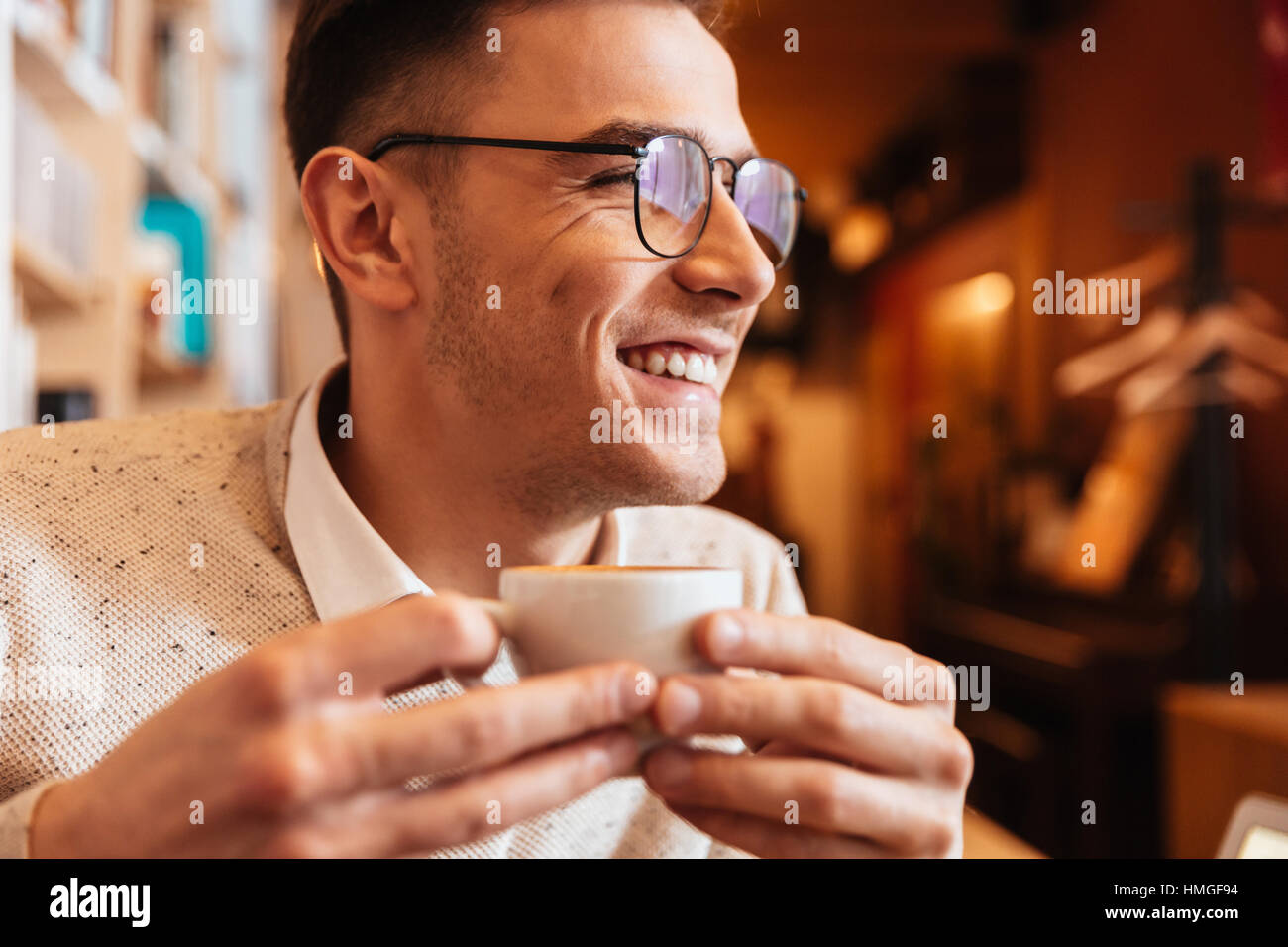 Picture of cheerful young man sitting in cafe while drinking coffee and ...