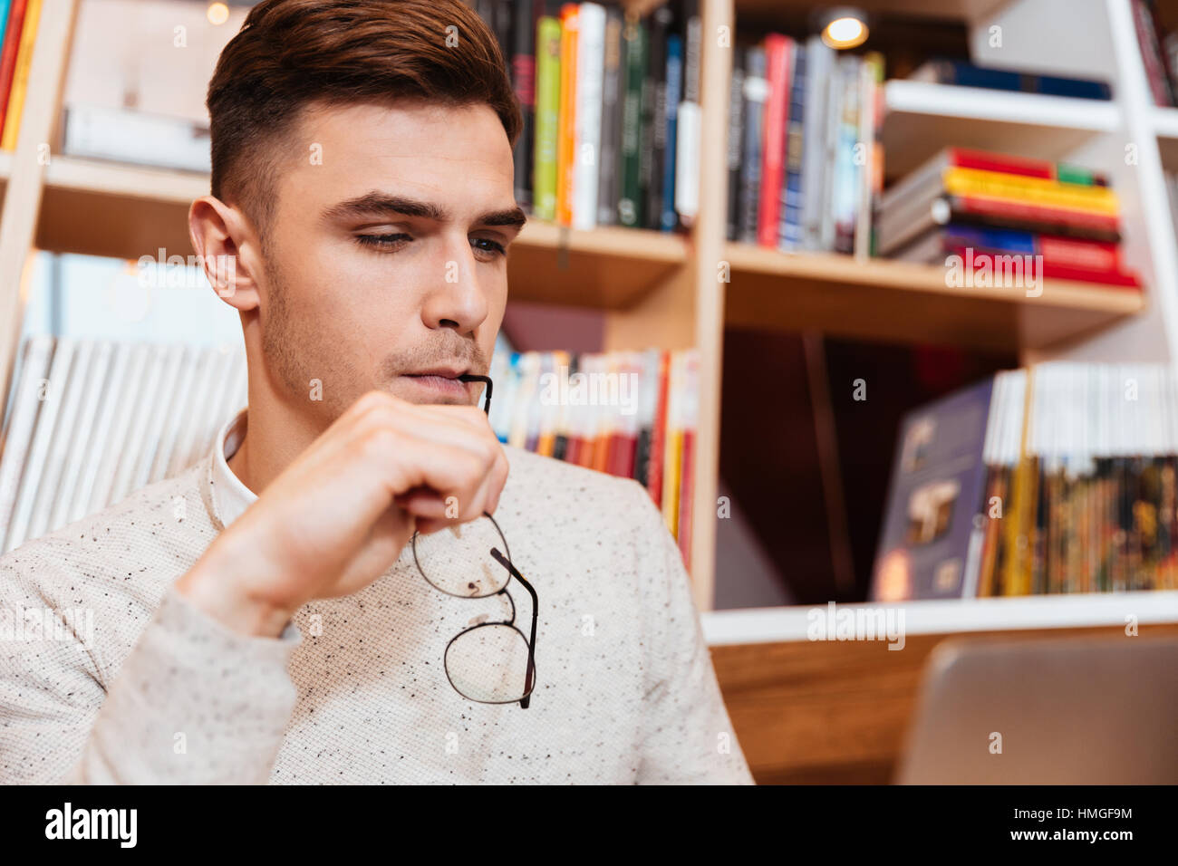 Picture of young man holding glasses while sitting in cafe and using ...