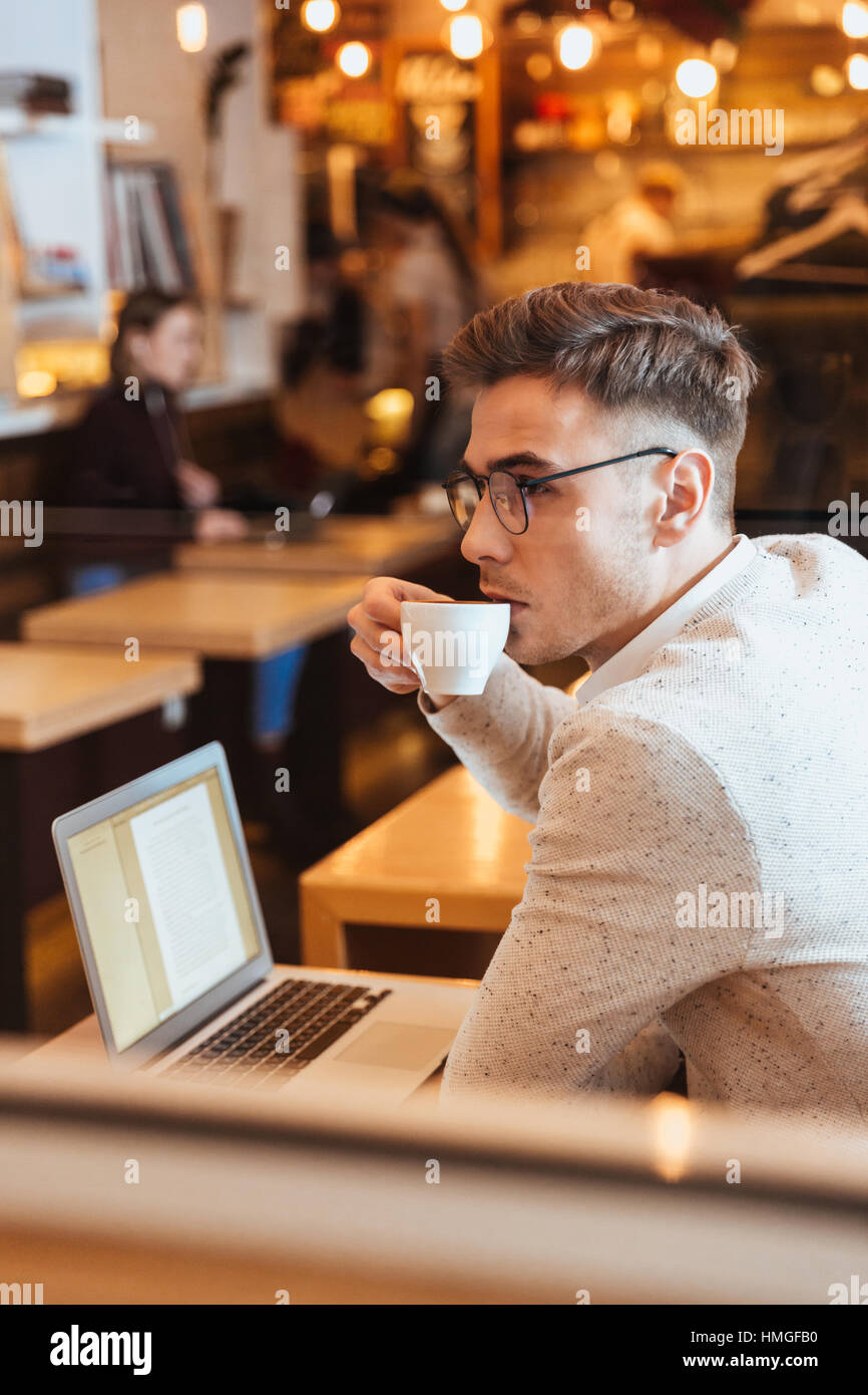 Picture of attractive young man sitting in cafe and chatting by laptop ...