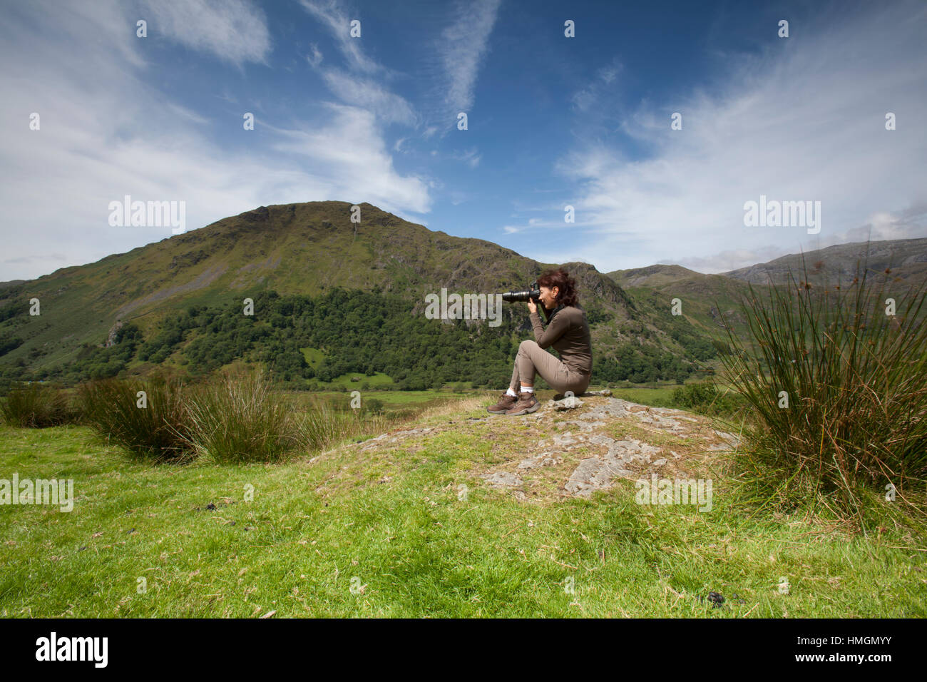 An attractive female / woman photographer, sitting on a small hill ...