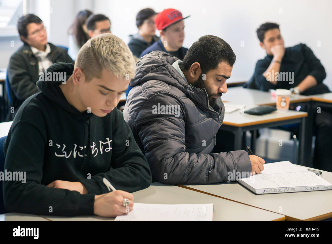 male students sit at a desk in a classroom taking notes during a lesson ...