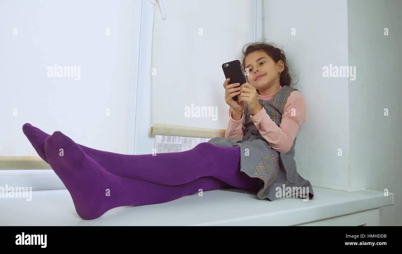 teen girl sitting on a window sill plays the online web game for ...