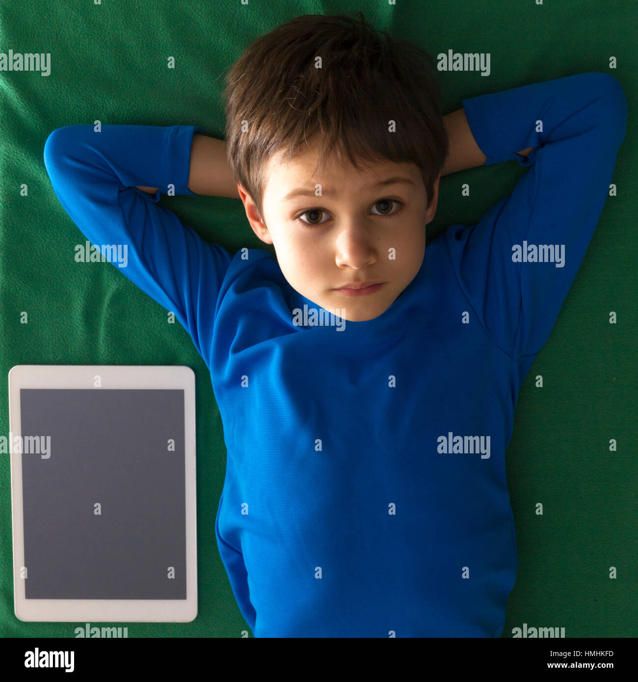 Kid with digital tablet computer at home. Boy lying on his bed and ...