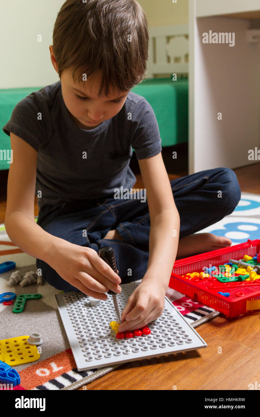 Concentrated kid playing with toys construction tool kit while sitting ...