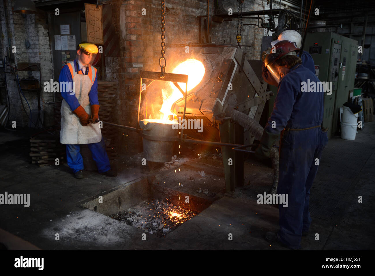 Foundrymen pour molten iron from an induction furnace into the ladel at ...