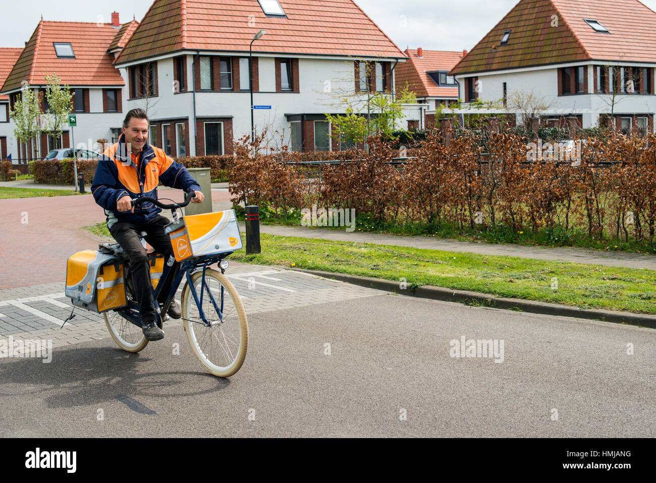 Empel, Netherlands. Postman on bike passing by in the village ...