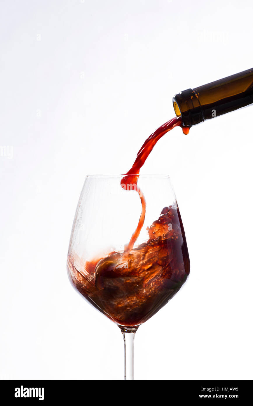 Vigorously wine poured from a bottle in a wine glass, on a white ...
