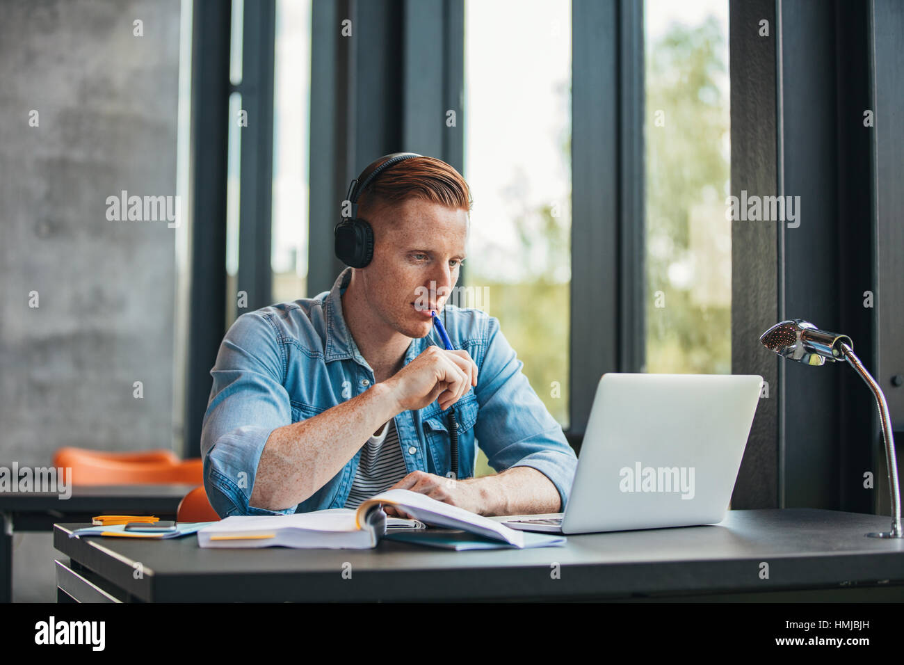 Shot of young man with headphones looking at laptop. University student ...