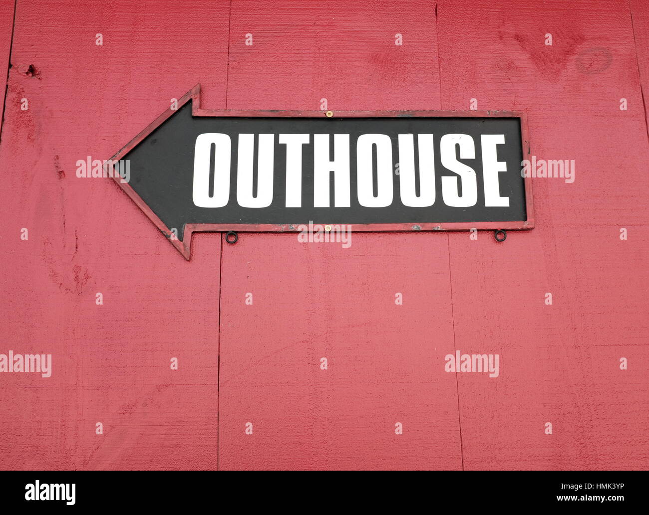 Sign pointing to outhouse on red wood Stock Photo - Alamy