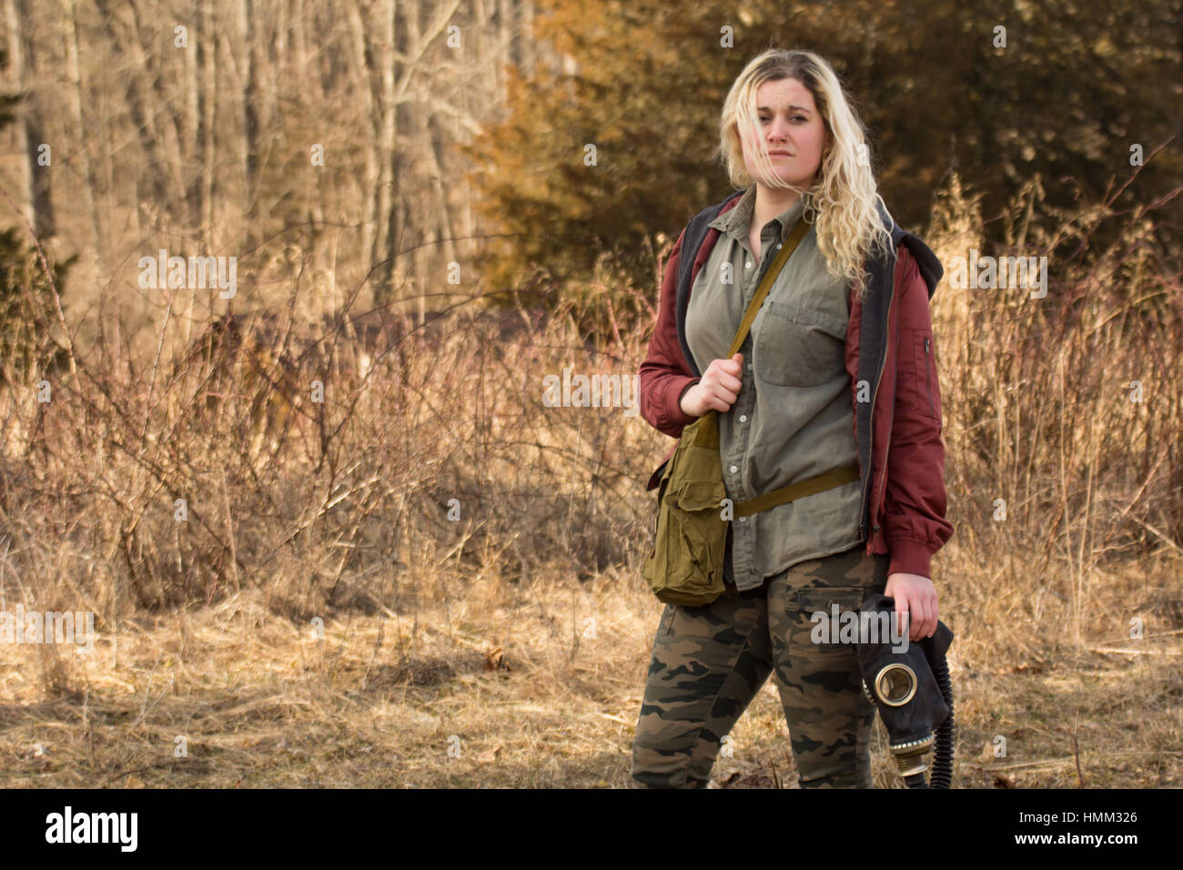 Worried pretty girl carrying authentic Russian gas mask through field ...