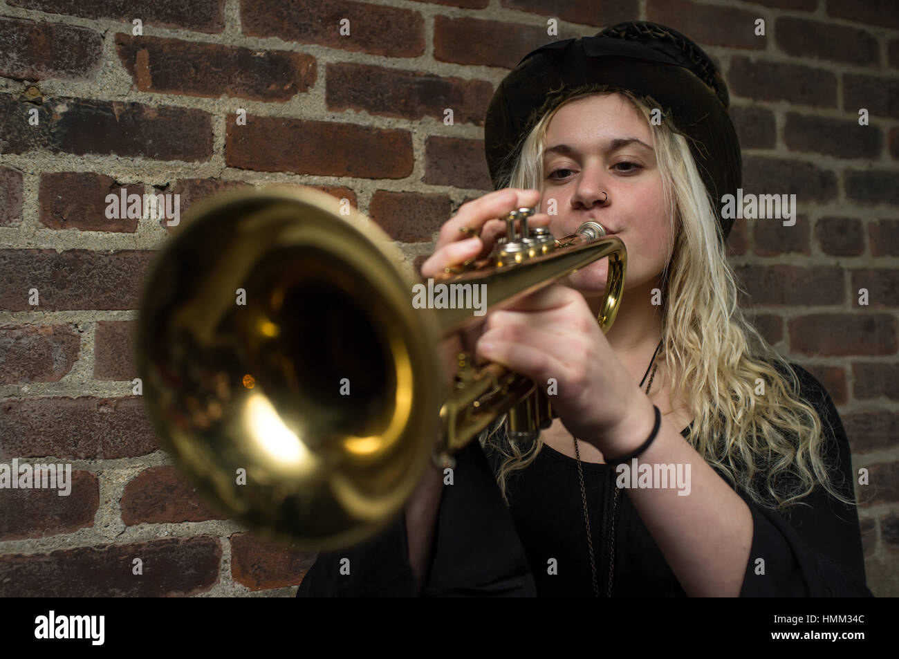Stylish blonde gypsy girl plays trumpet by brick wall Stock Photo - Alamy