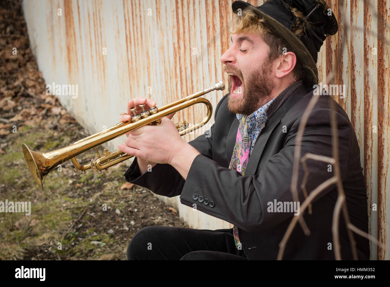 Stylish bearded gypsy plays trumpet by rusty fence Stock Photo - Alamy