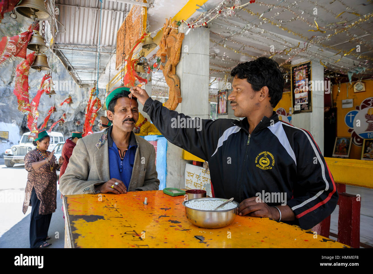 Indian men in a temple, one applying a red tilaka (dot) to the other’s ...