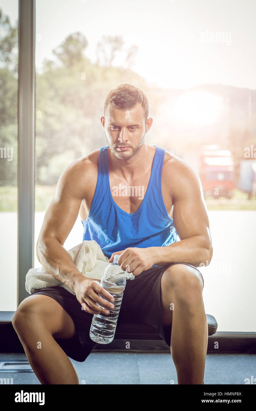 Young adult bodybuilder drinking water from bottle on bench after ...