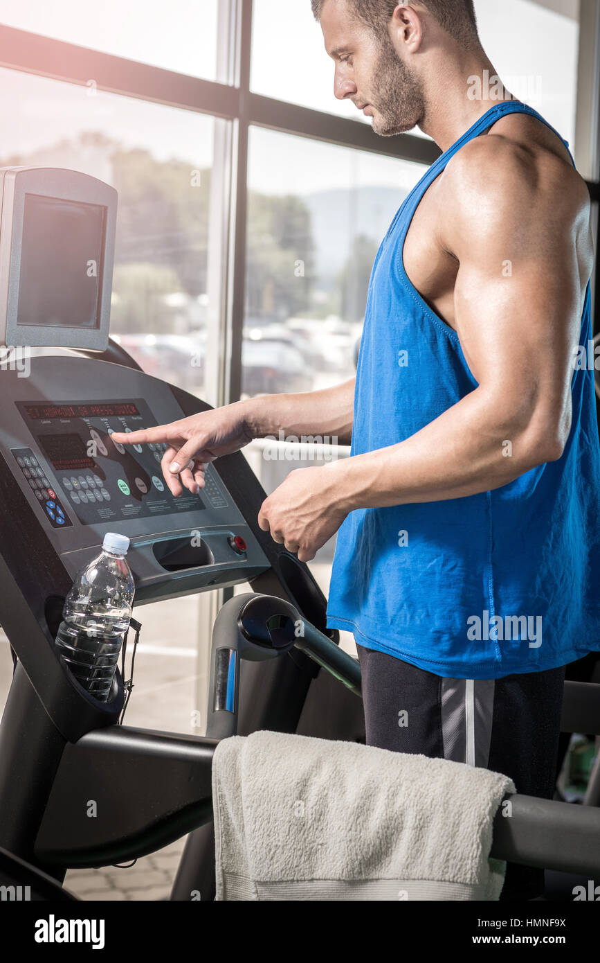 Young adult man setting control panel of treadmill before doing ...