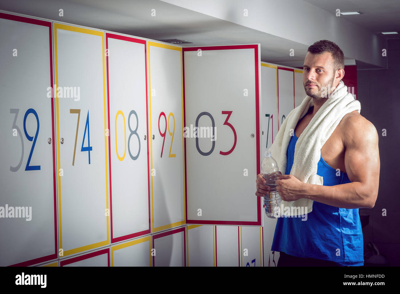 Young adult fit man standing in locker room and opening locker door ...