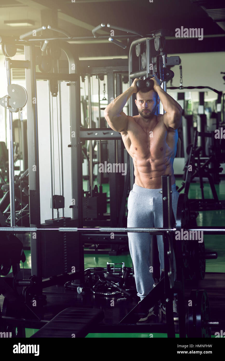 Young adult bodybuilder doing triceps overhead extension rope exercise ...
