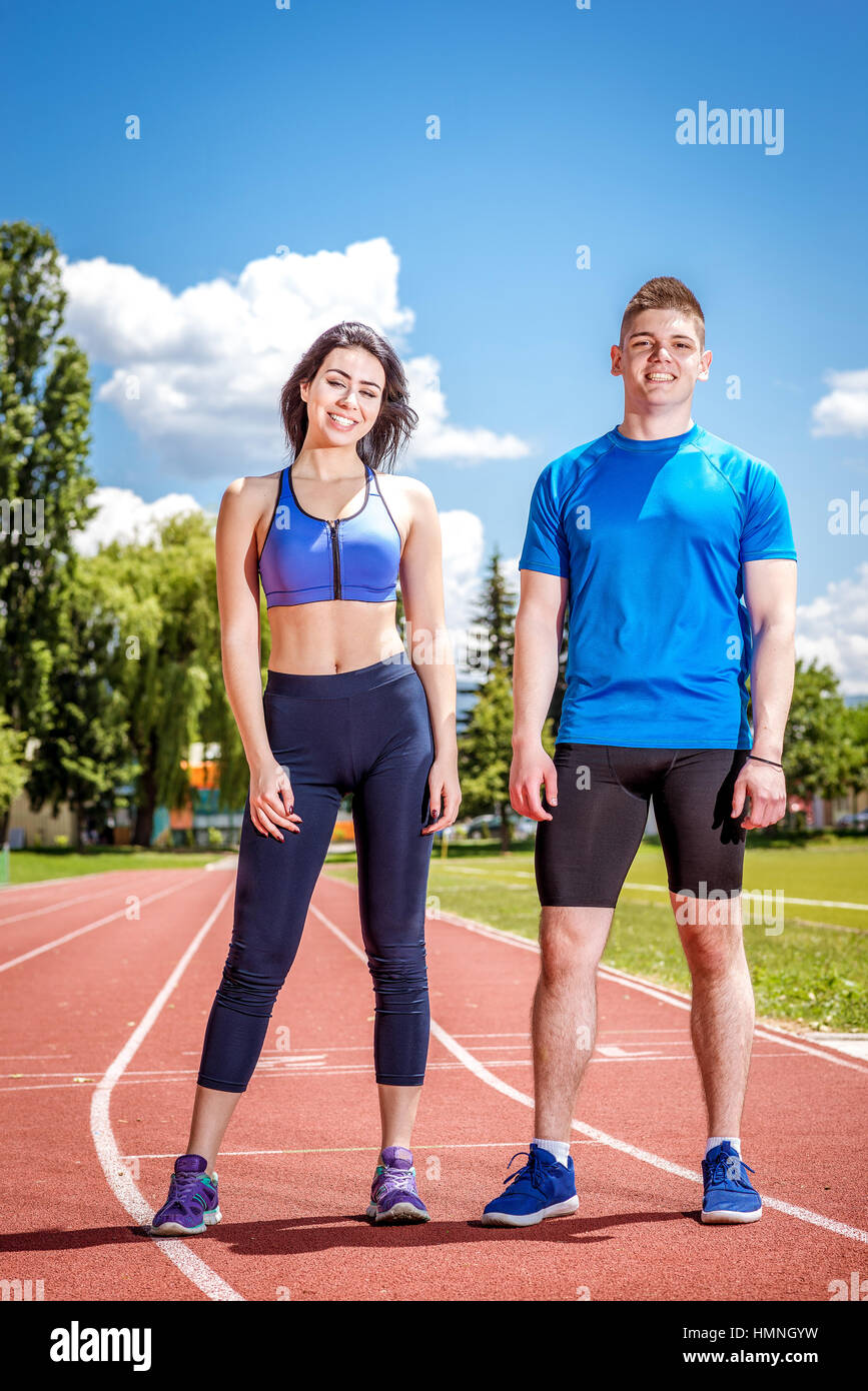 Young adult couple standing and talking on athletics track field during ...