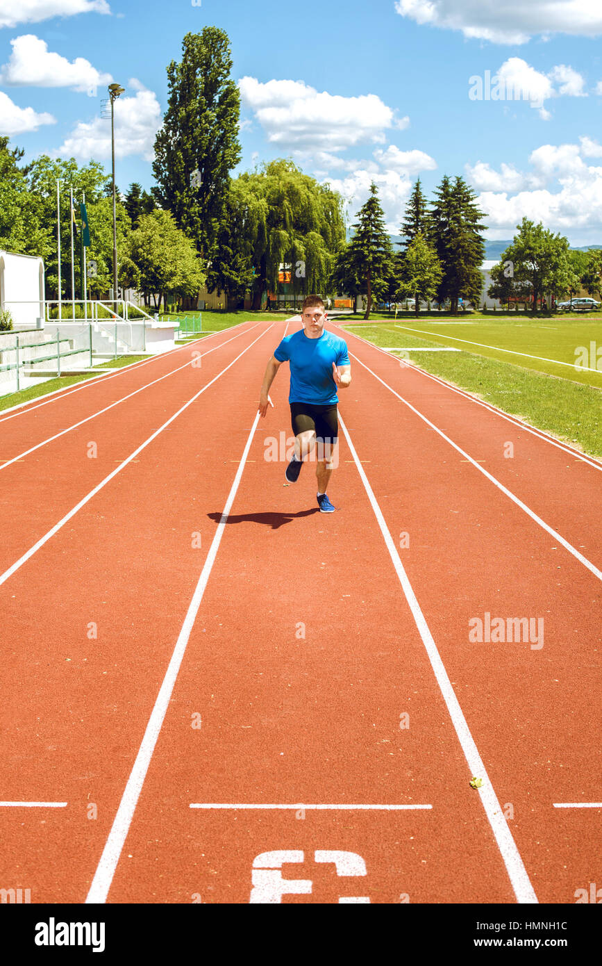 Running fast on athletic track. Young adult man sprinting fast during ...