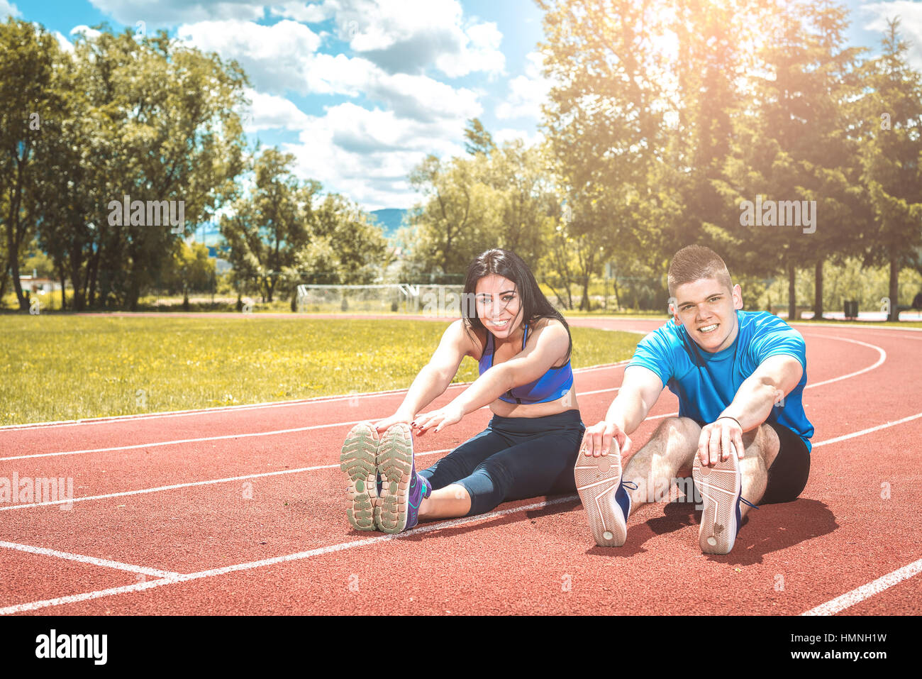Two young vital people doing stretching relaxing exercises on athletics ...