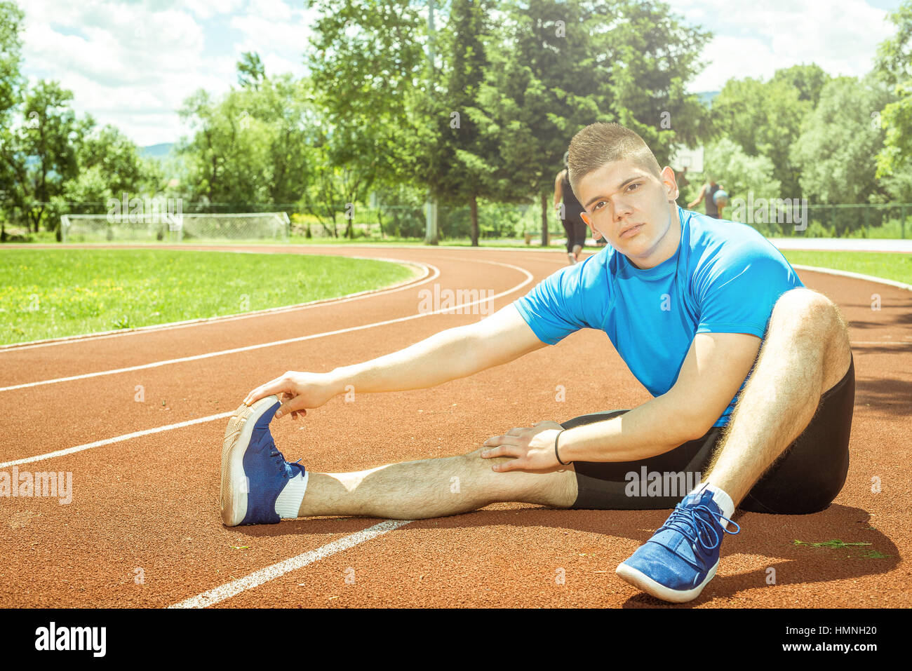 Man doing stretching exercises on open air athletics track field during ...