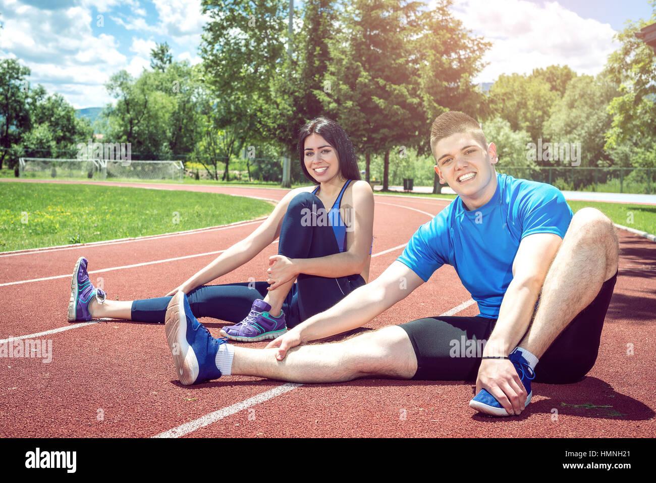 Two young vital people doing stretching relaxing exercises on athletics ...